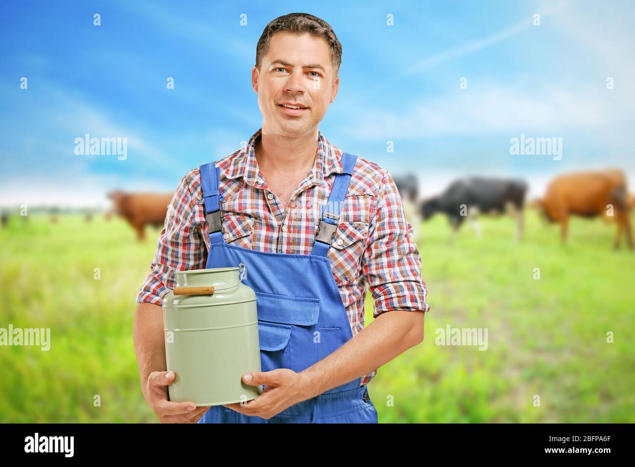 Handsome milkman with can on blurred cow pasture background. Dairy ...