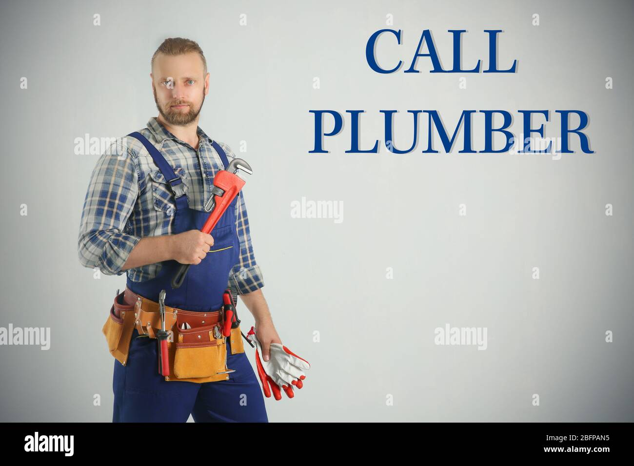 Call Plumber. Handsome plumber with pipe wrench and gloves on light ...