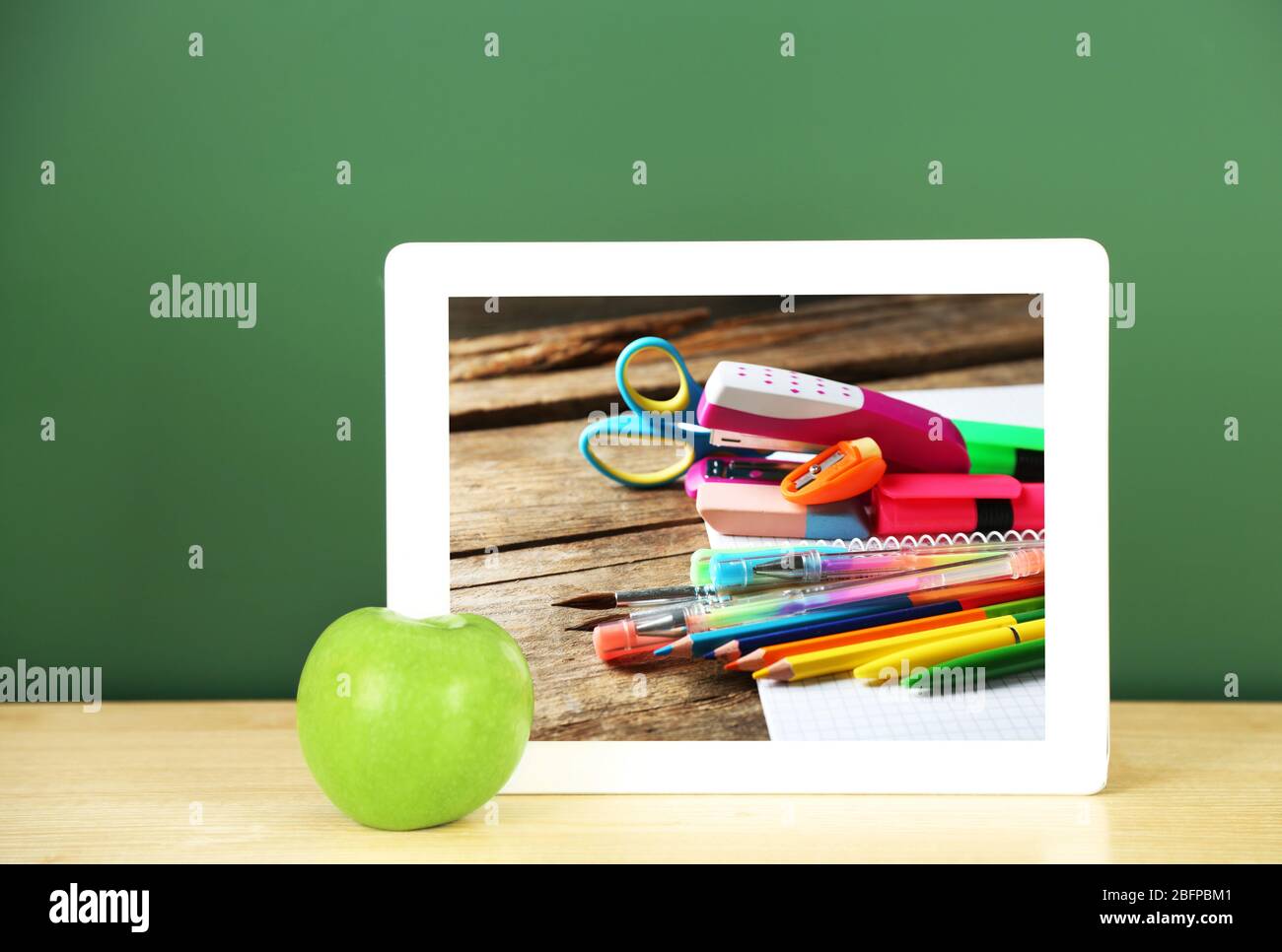 Tablet with stationery wallpaper on screen against chalkboard ...