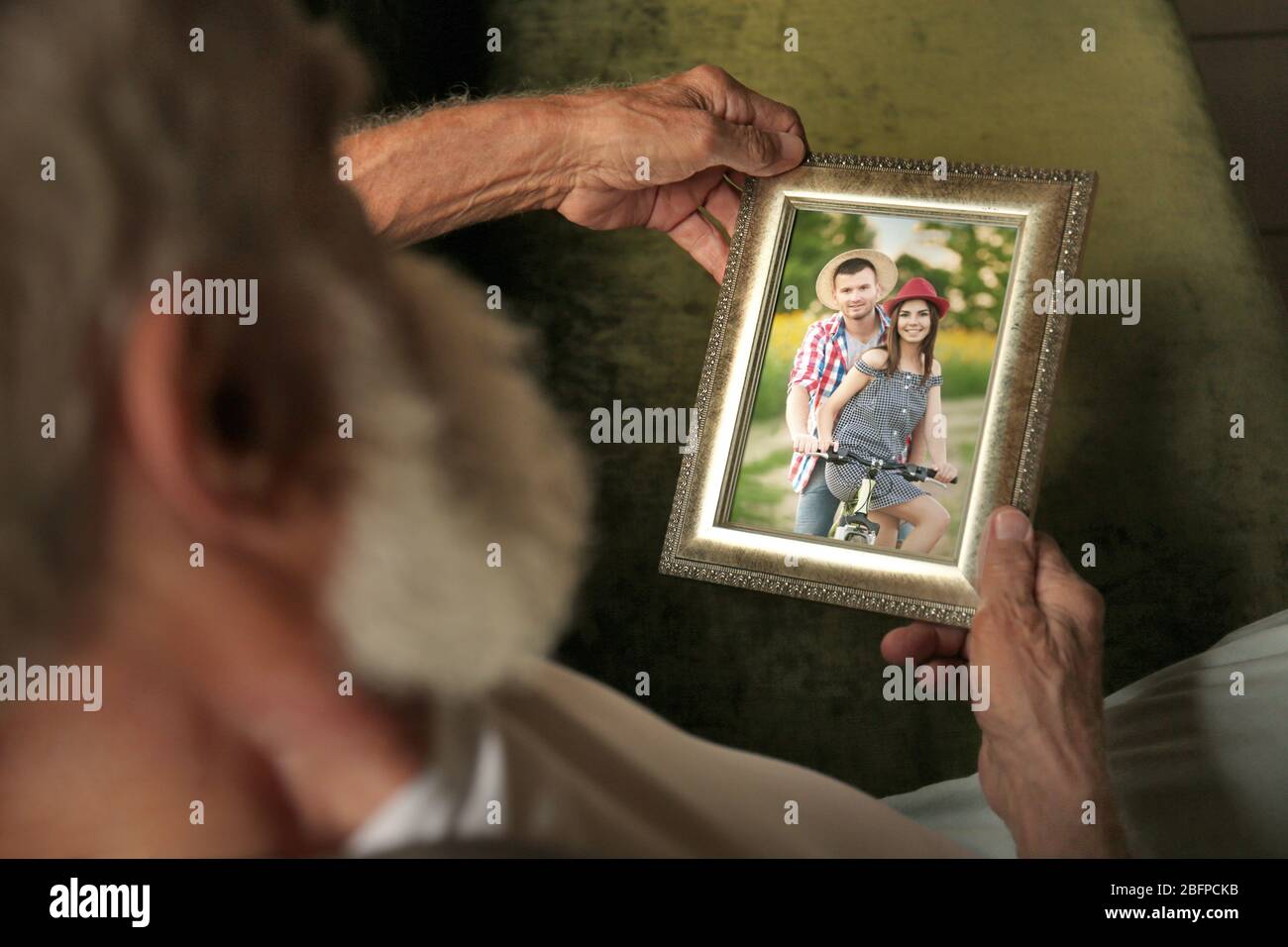 Elderly man holding photo frame with picture of young couple. Happy ...