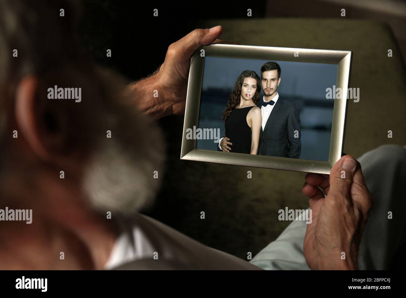 Elderly man holding photo frame with picture of young couple. Happy ...