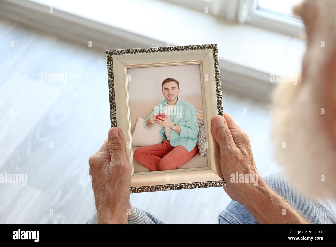 Elderly man holding photo frame with picture of grandson. Happy ...