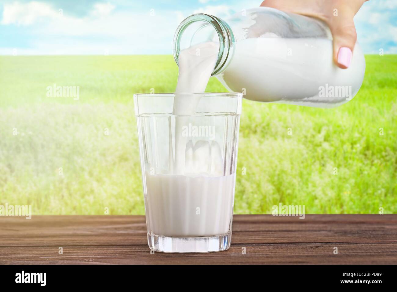 Female hand pouring milk into glass against blurred nature background ...