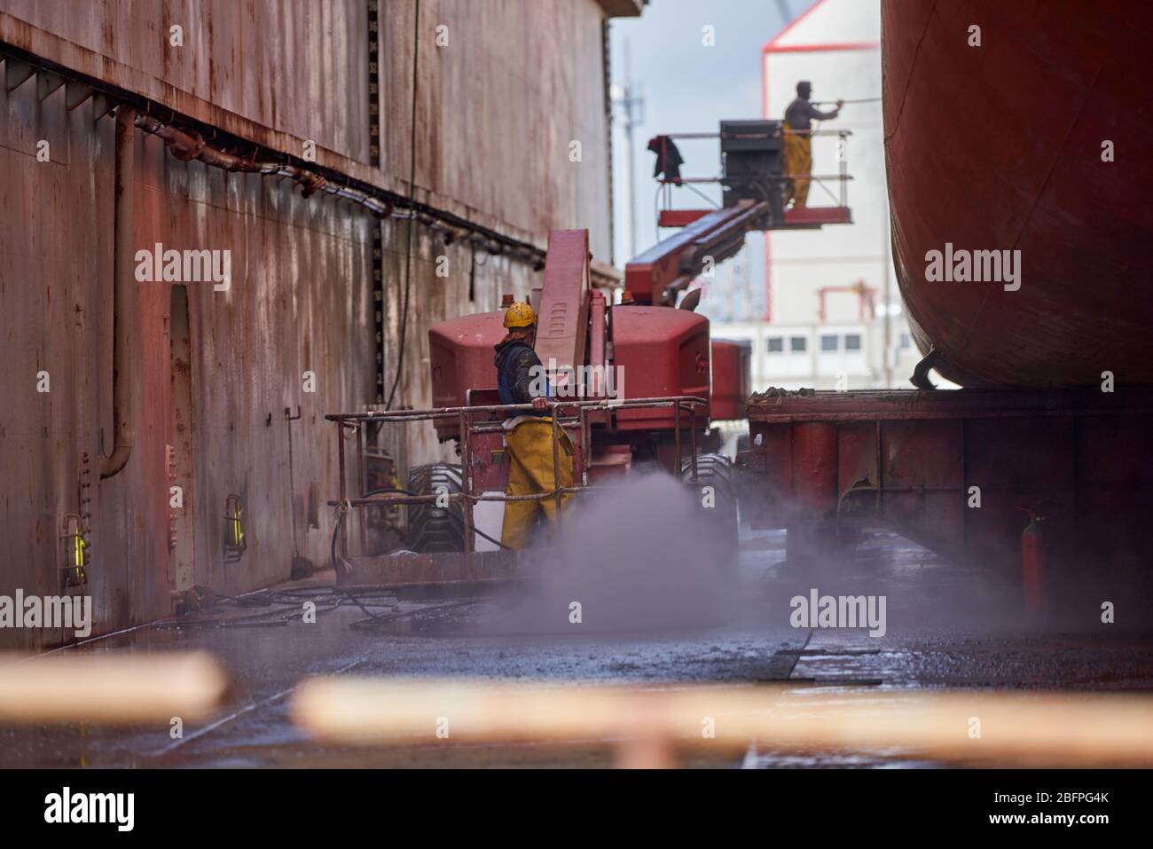 A crane with a worker doing work on ship in background a second worker ...