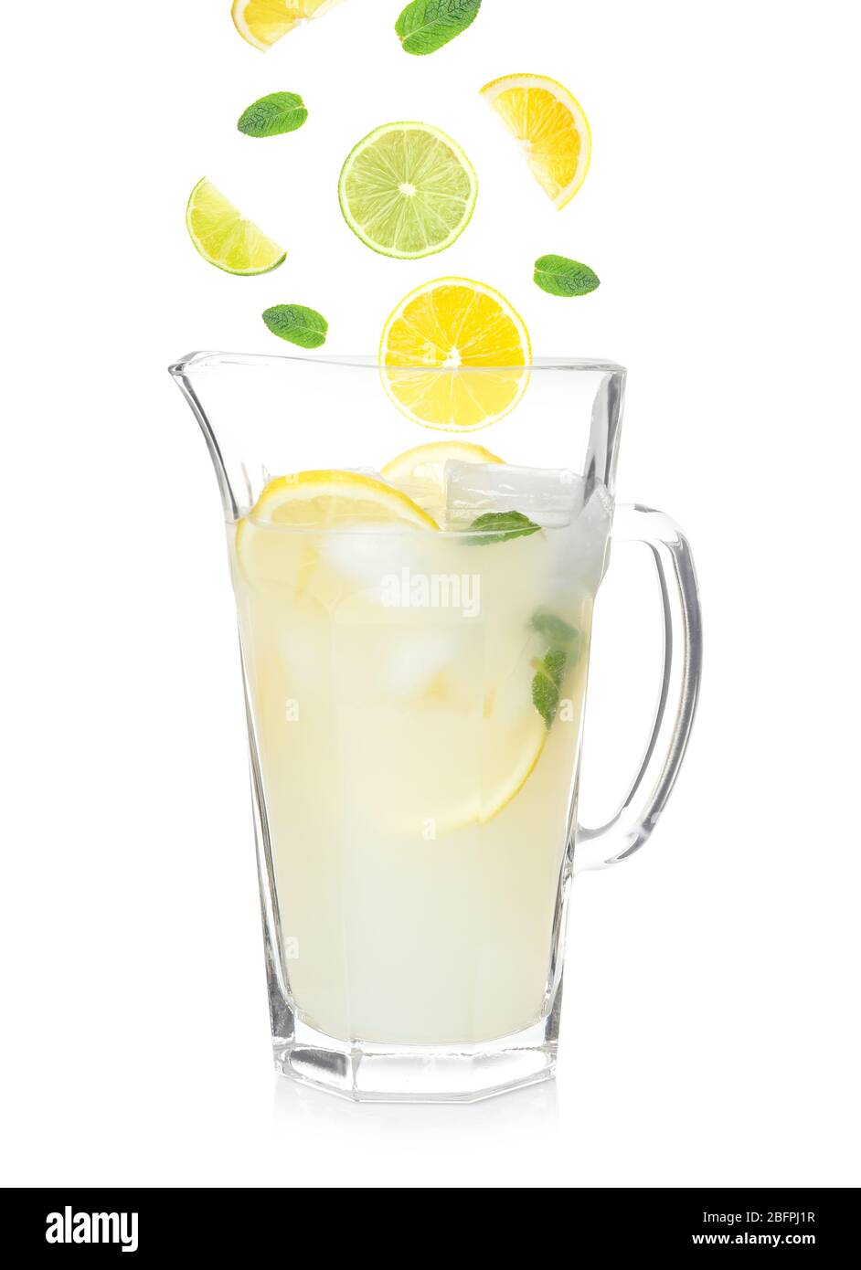 Falling fruit slices into glass jug with lemonade on white background ...