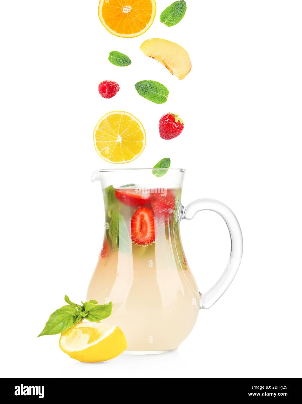 Falling fruit slices and berries into glass jug with lemonade on white ...