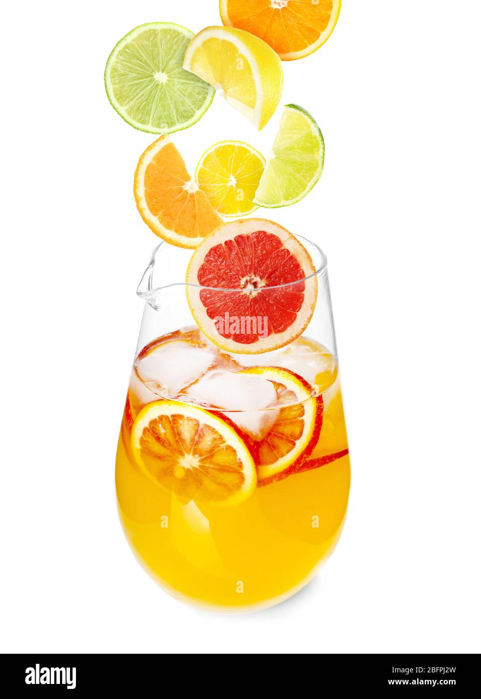 Falling fruit slices into glass jug with lemonade on white background ...
