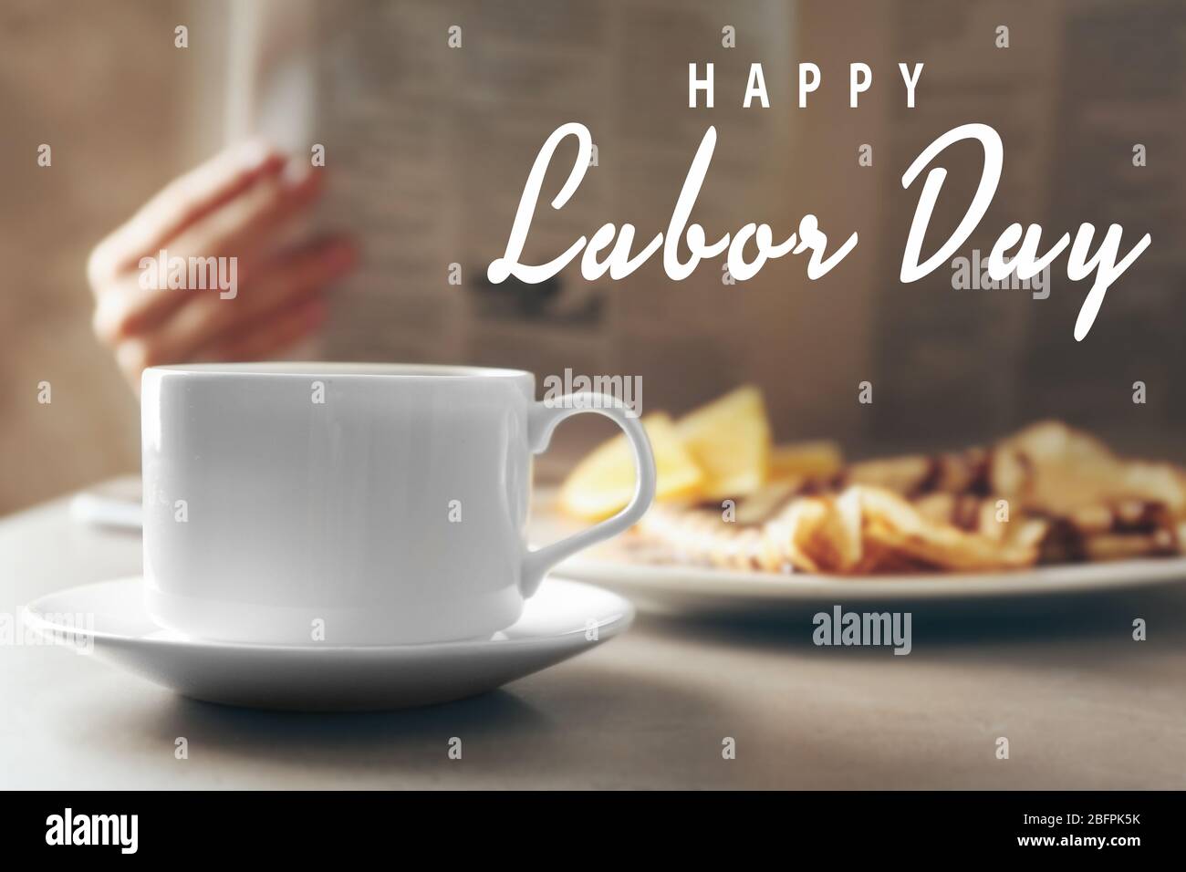 Cup of coffee and breakfast on table. Text HAPPY LABOR DAY on blurred ...