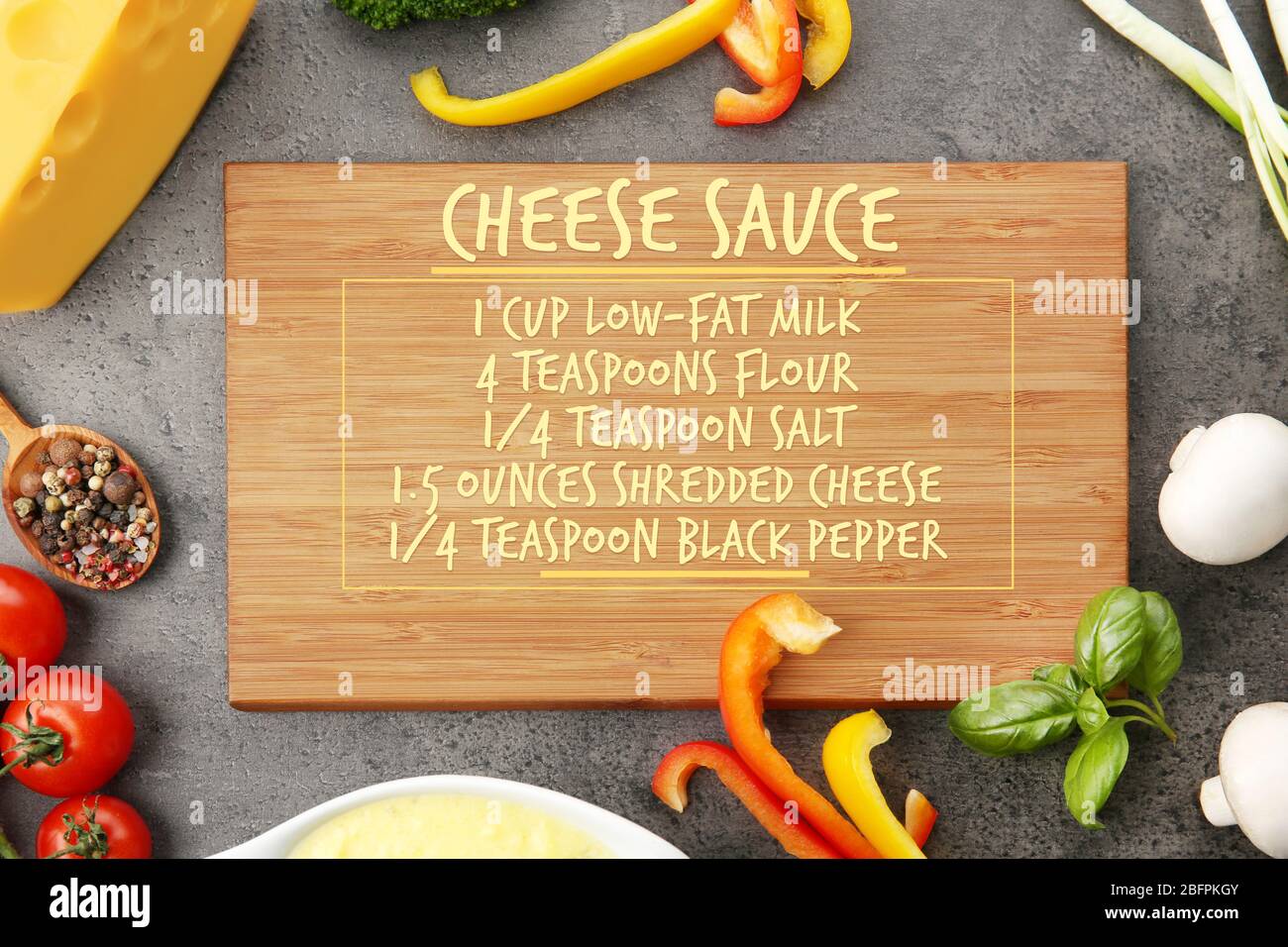 Wooden board with cheese sauce recipe and food products on gray ...