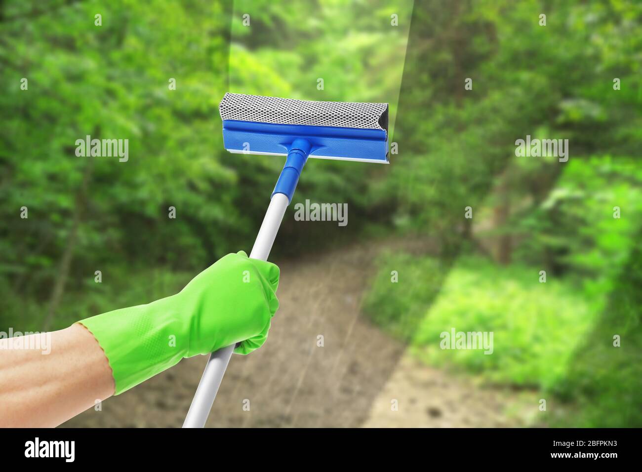 Man removing dirt from glass with squeegee. View of landscape through ...
