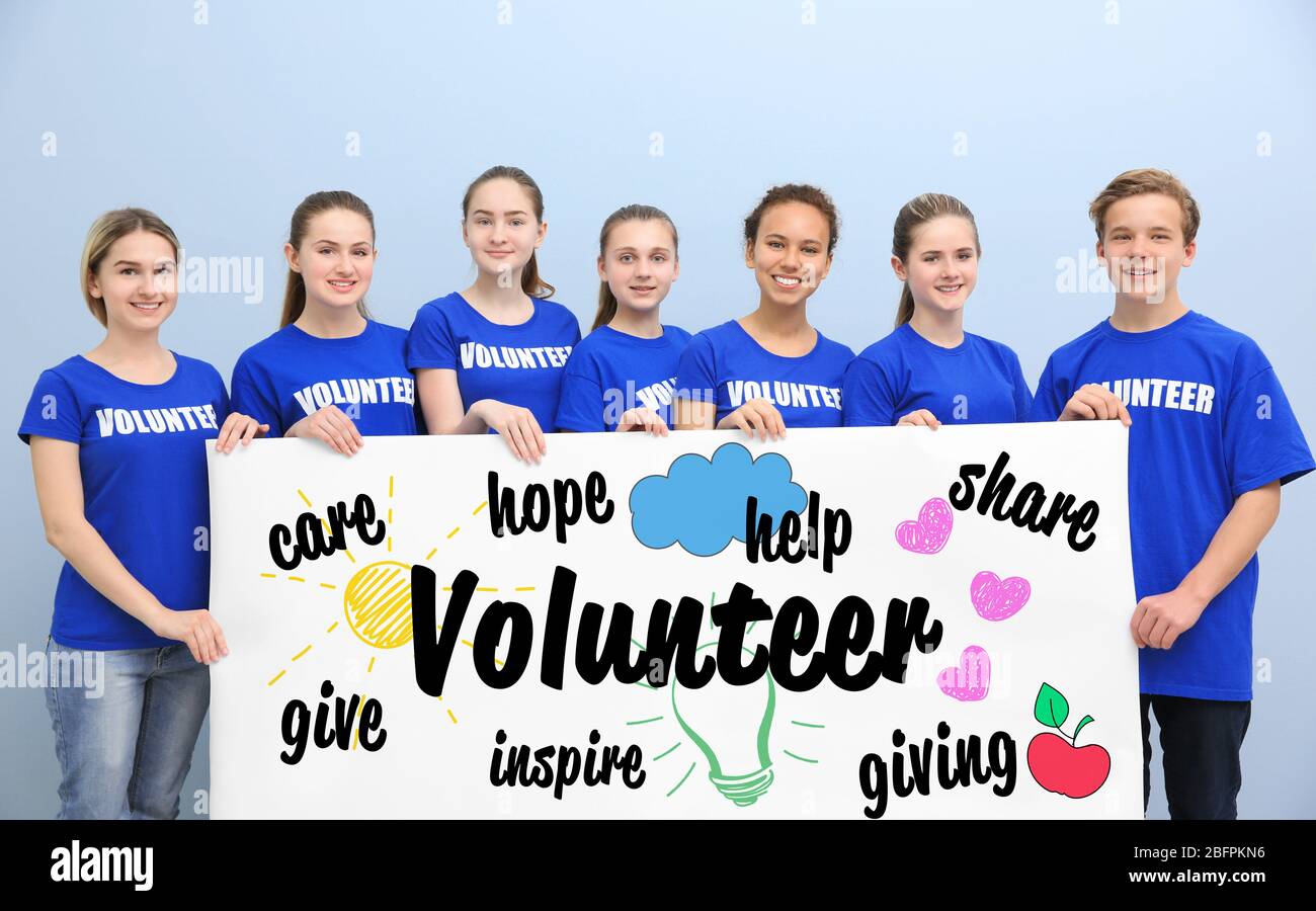 Group of teens holding poster with word VOLUNTEER on color background ...