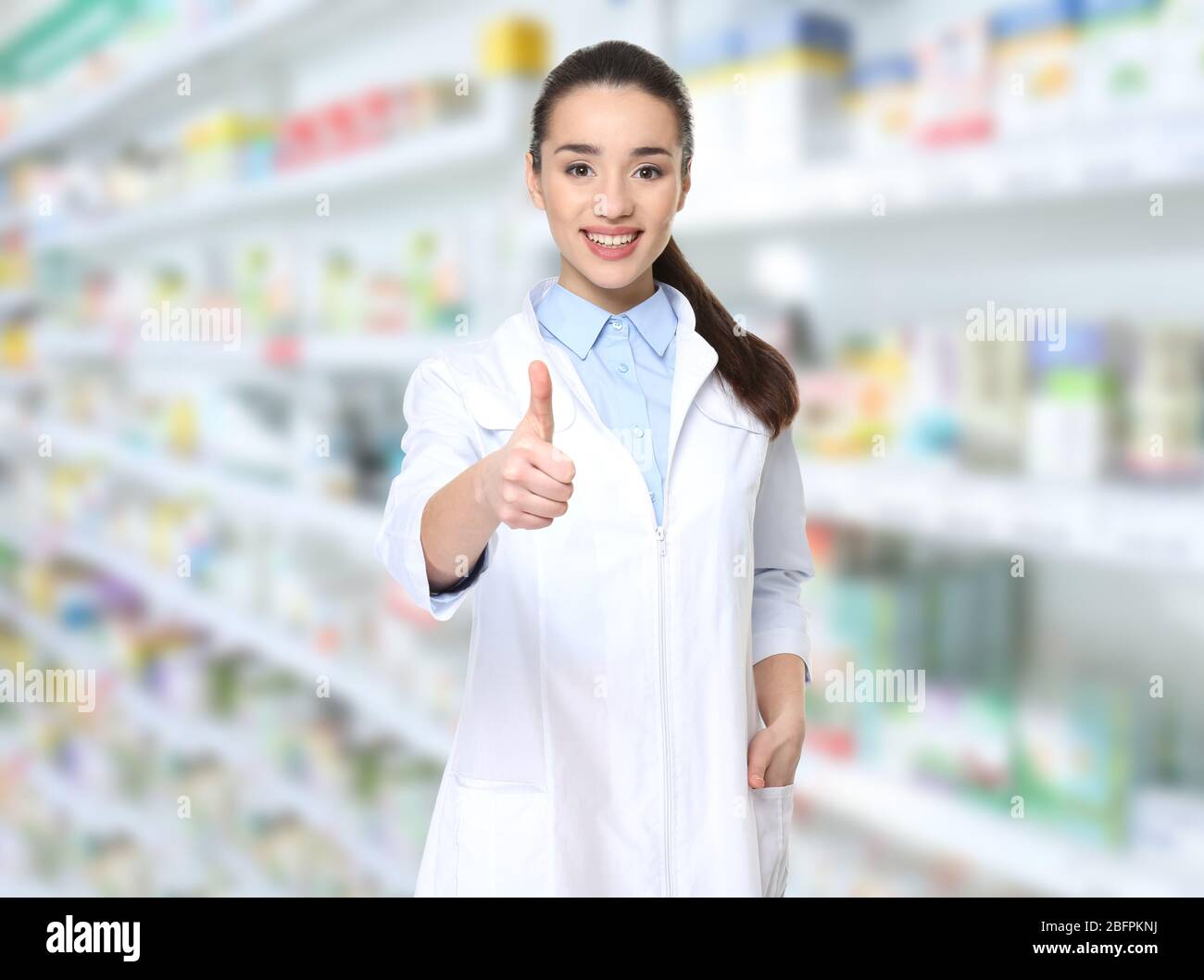 Young female pharmacist at work. Blurred shelves with pharmaceutical ...