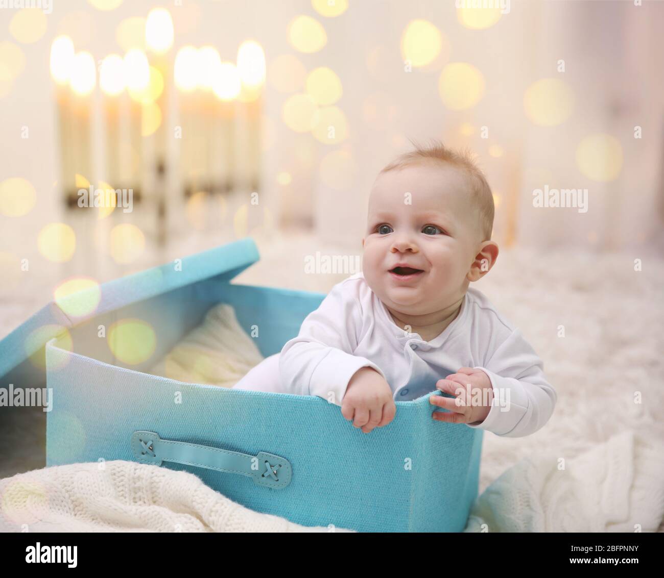 Little child in box on blurred festive lights background. Baby's First ...