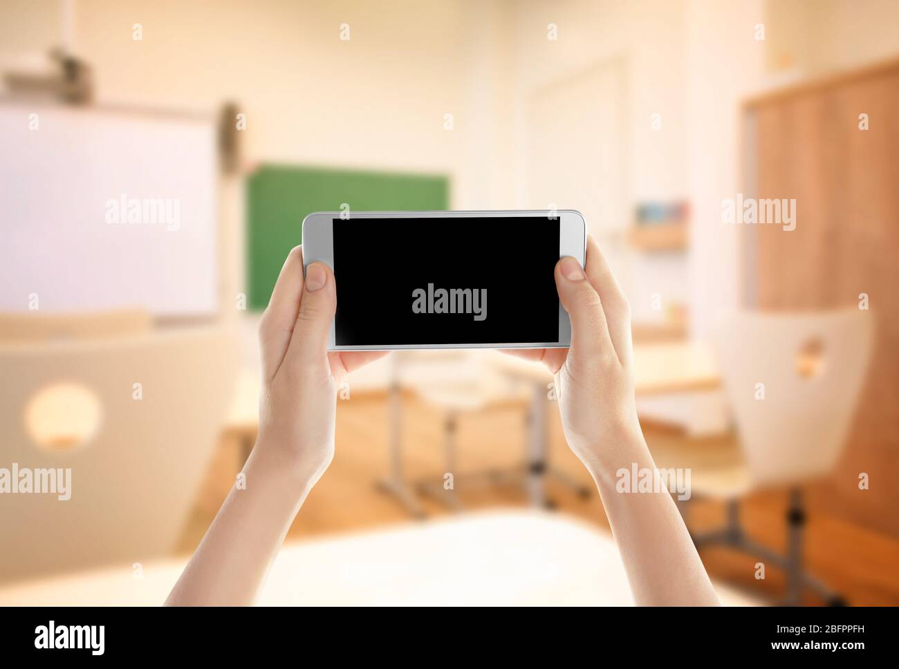 Teacher holding smartphone with blank screen and classroom on ...