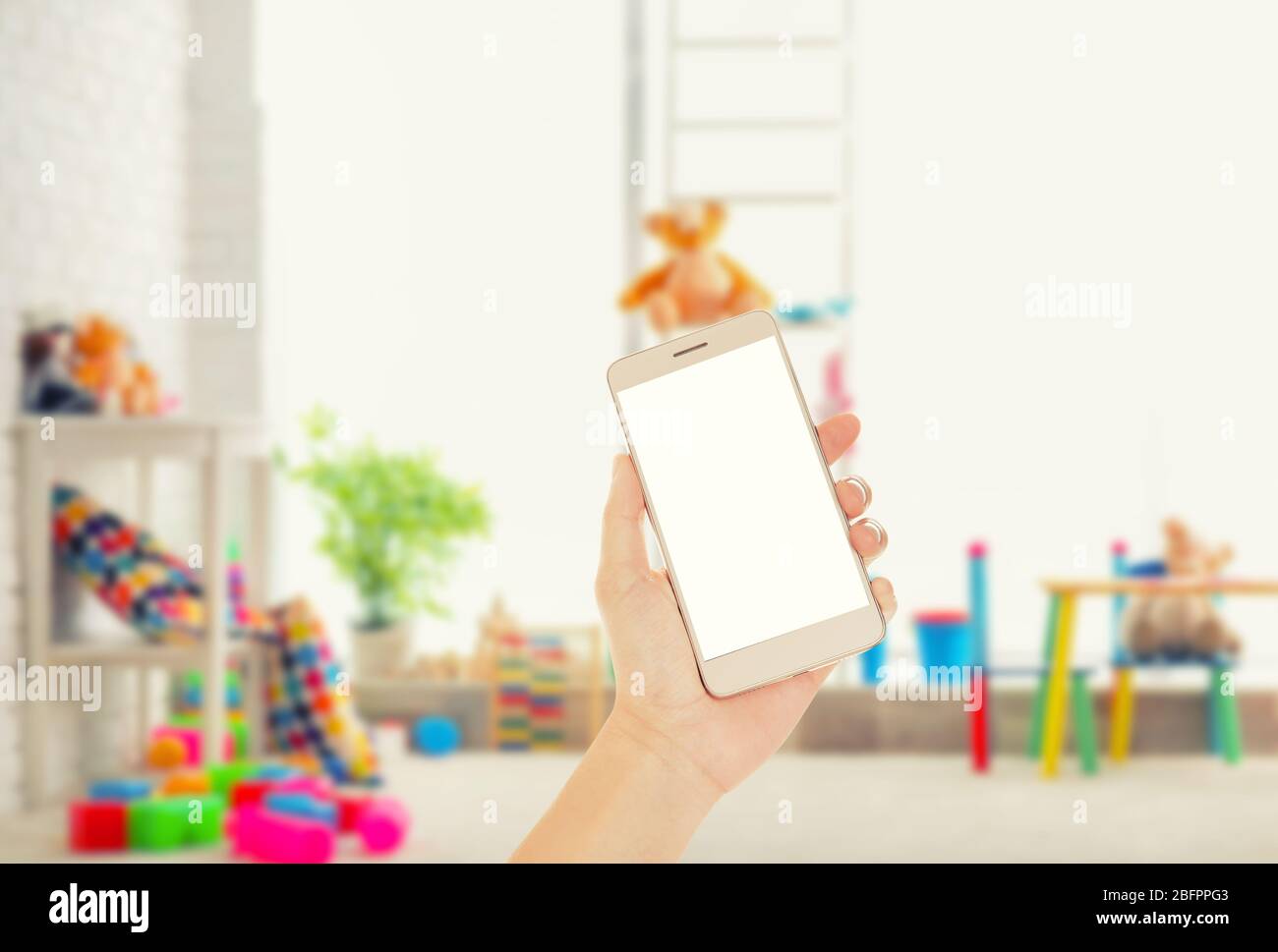Teacher holding smartphone with blank screen and play room on ...