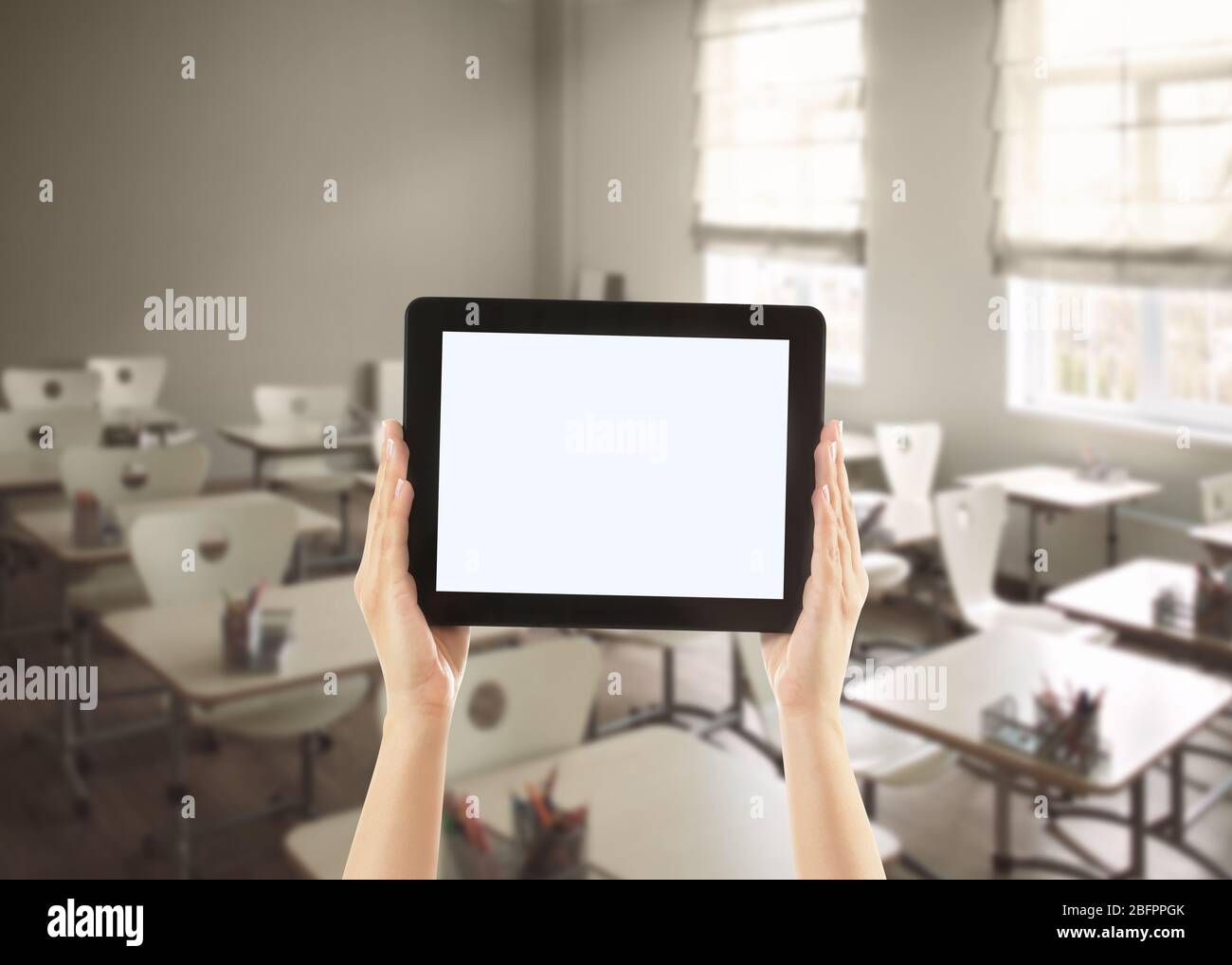 Teacher holding tablet with blank screen and classroom on background ...