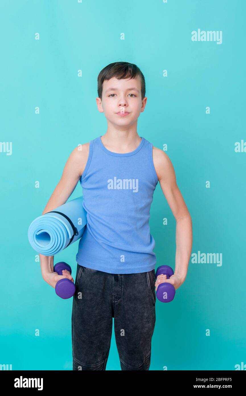Portrait of a handsome teenage sport boy with dumbbells and gym mat ...