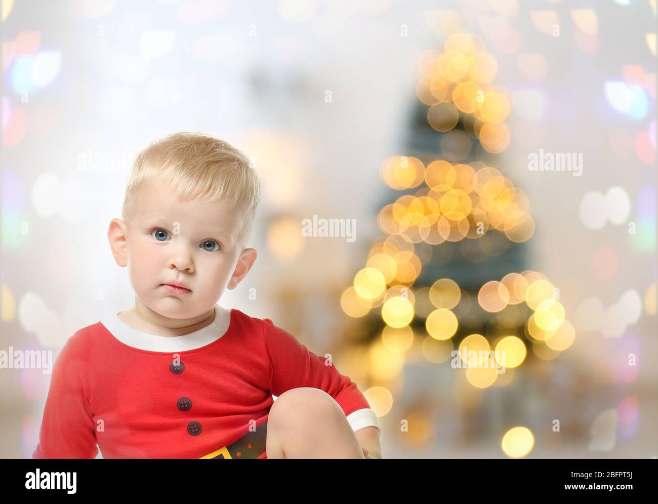 Cute baby in costume of Santa's helper and Christmas tree on background ...