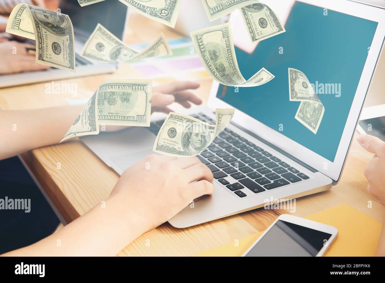 Money flying out of laptop while man using it at table in office Stock ...