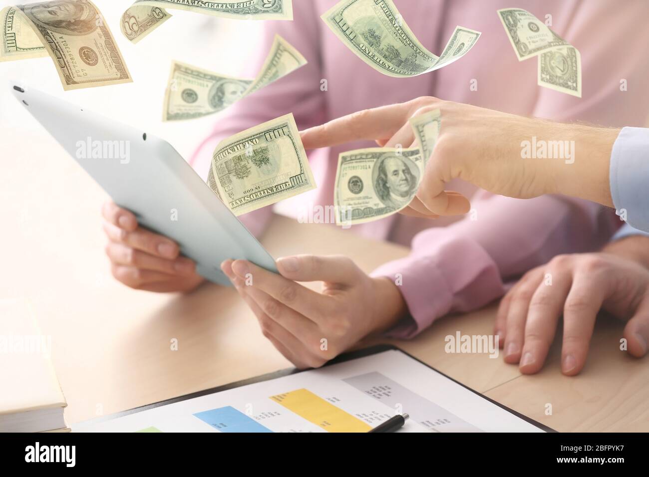 Money flying out of tablet while people using it at table in office ...
