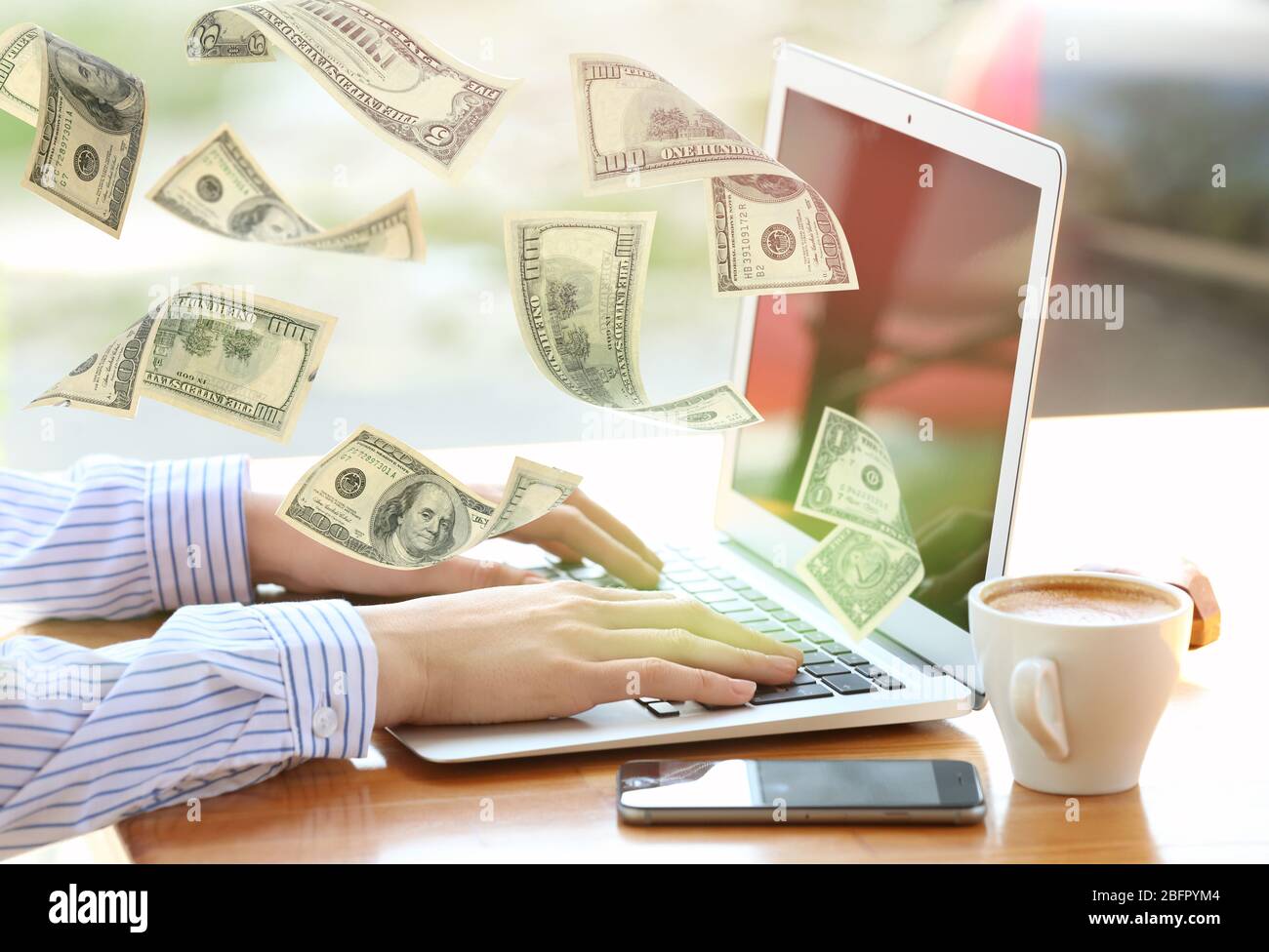 Money flying out of laptop while woman using it at table in office ...