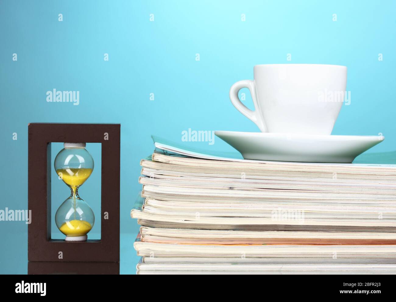 stack of magazines, cup and hourglass on blue background Stock Photo ...