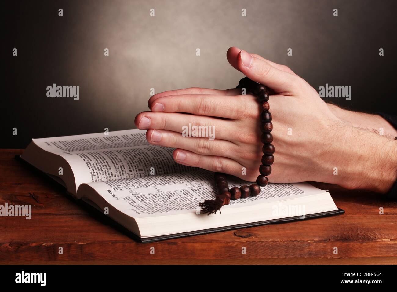 Hands holding wooden rosary over open russian holy bible on grey ...