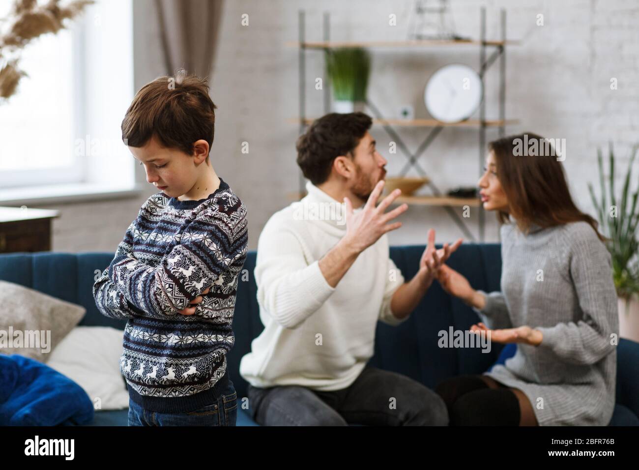 Sad little boy feels upset while his parents fighting at background ...