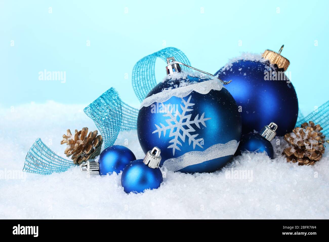 beautiful blue Christmas balls and cones in snow on blue background ...