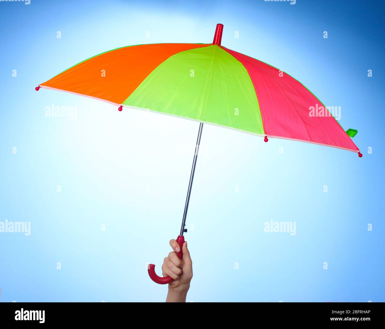 Multi-colored umbrella in hand on blue background Stock Photo - Alamy