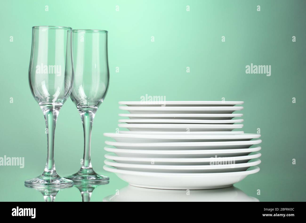 Clean plates and glasses on green background Stock Photo - Alamy