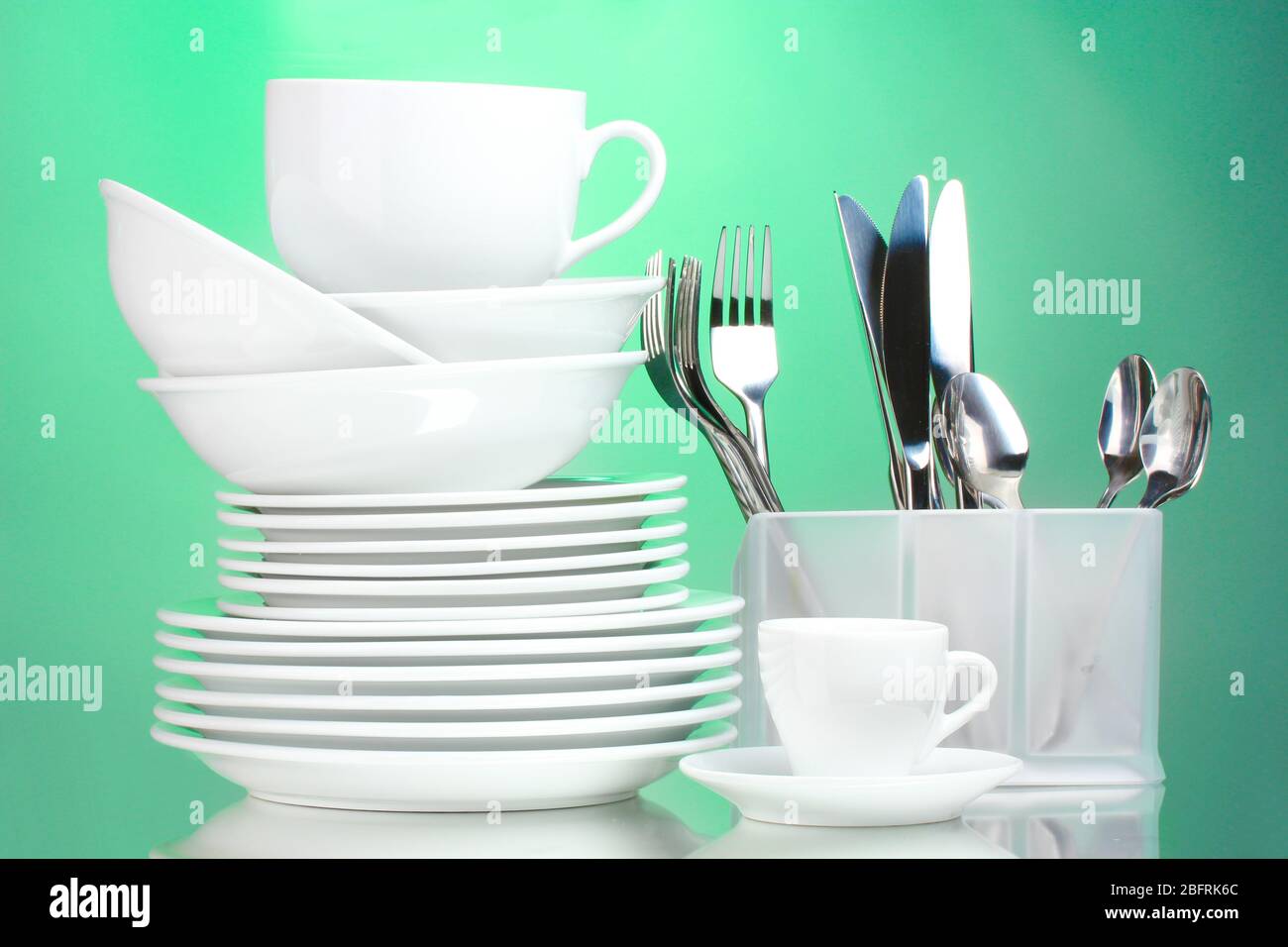 Clean plates, cups and cutlery on green background Stock Photo - Alamy