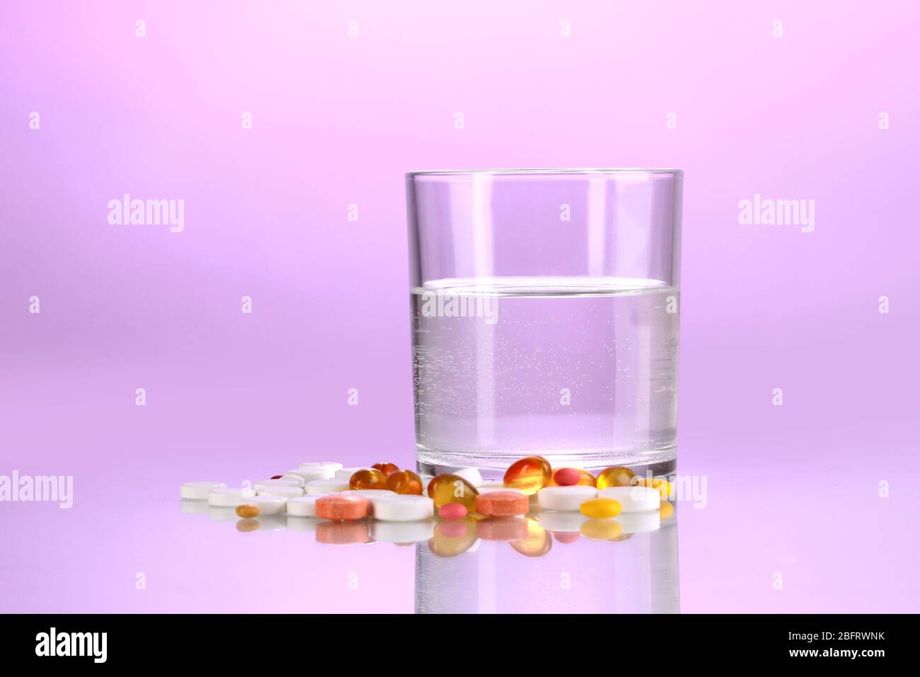 Glass of water and pills on purple background Stock Photo - Alamy