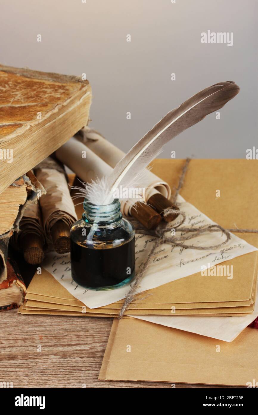 old books, scrolls, feather pen and inkwell on wooden table on grey ...