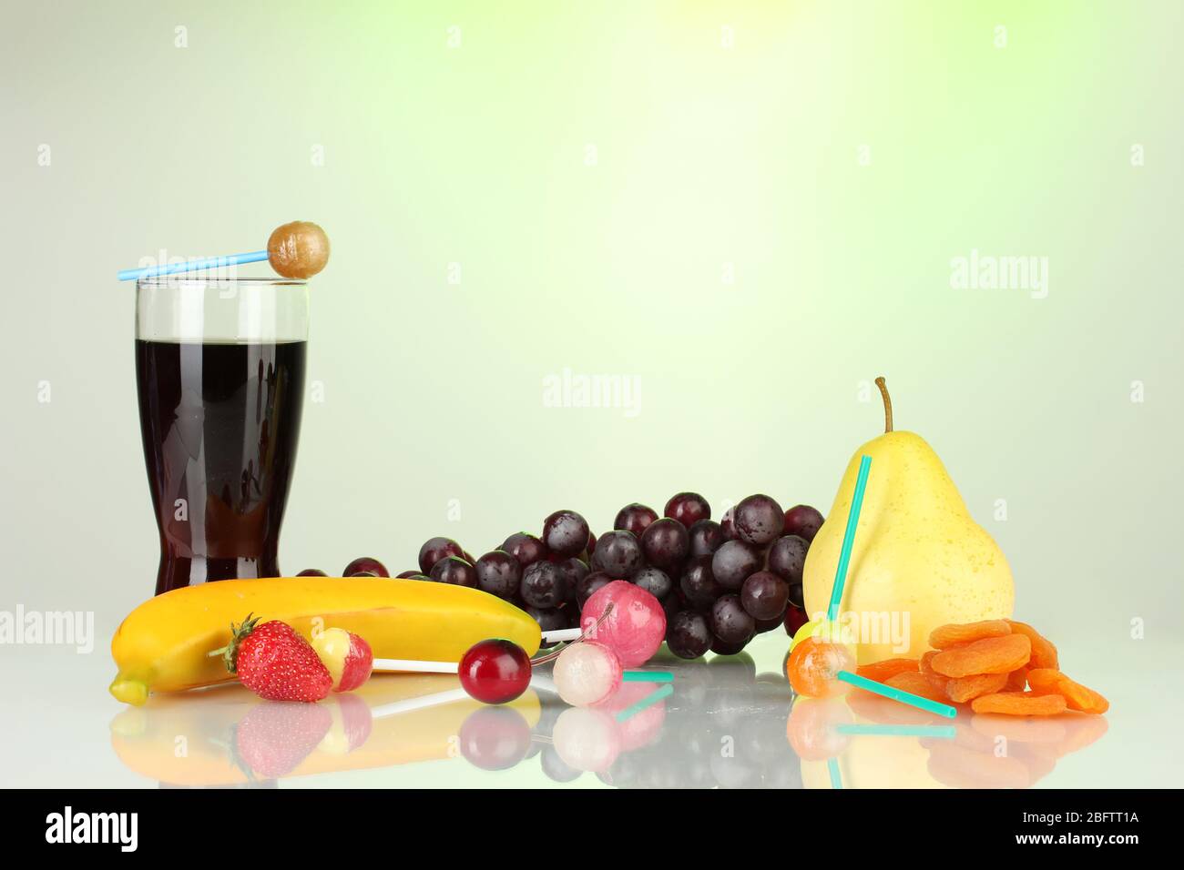 The composition of the lollipops, fruit and a glass of cola on green ...