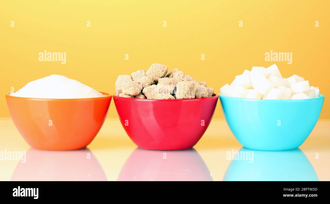 Colorful bowls with different types of sugar on a bright background ...