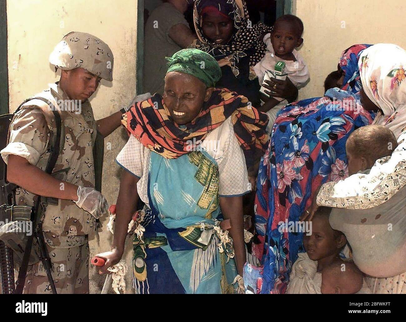 1993 - A US Marine helps a Somali woman on crutches from a clinic in Mogadishu, Somalia, where ...