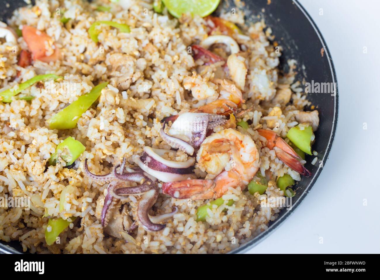 Asian fried rice with tiger prawn shrimp and seafood in pan on white ...