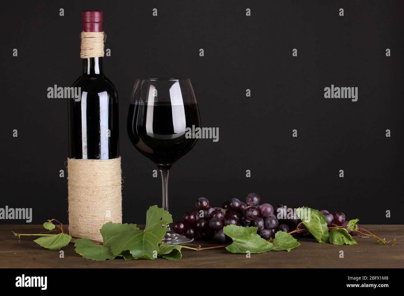 bottle of wine with grape leaves on wooden table on black background ...