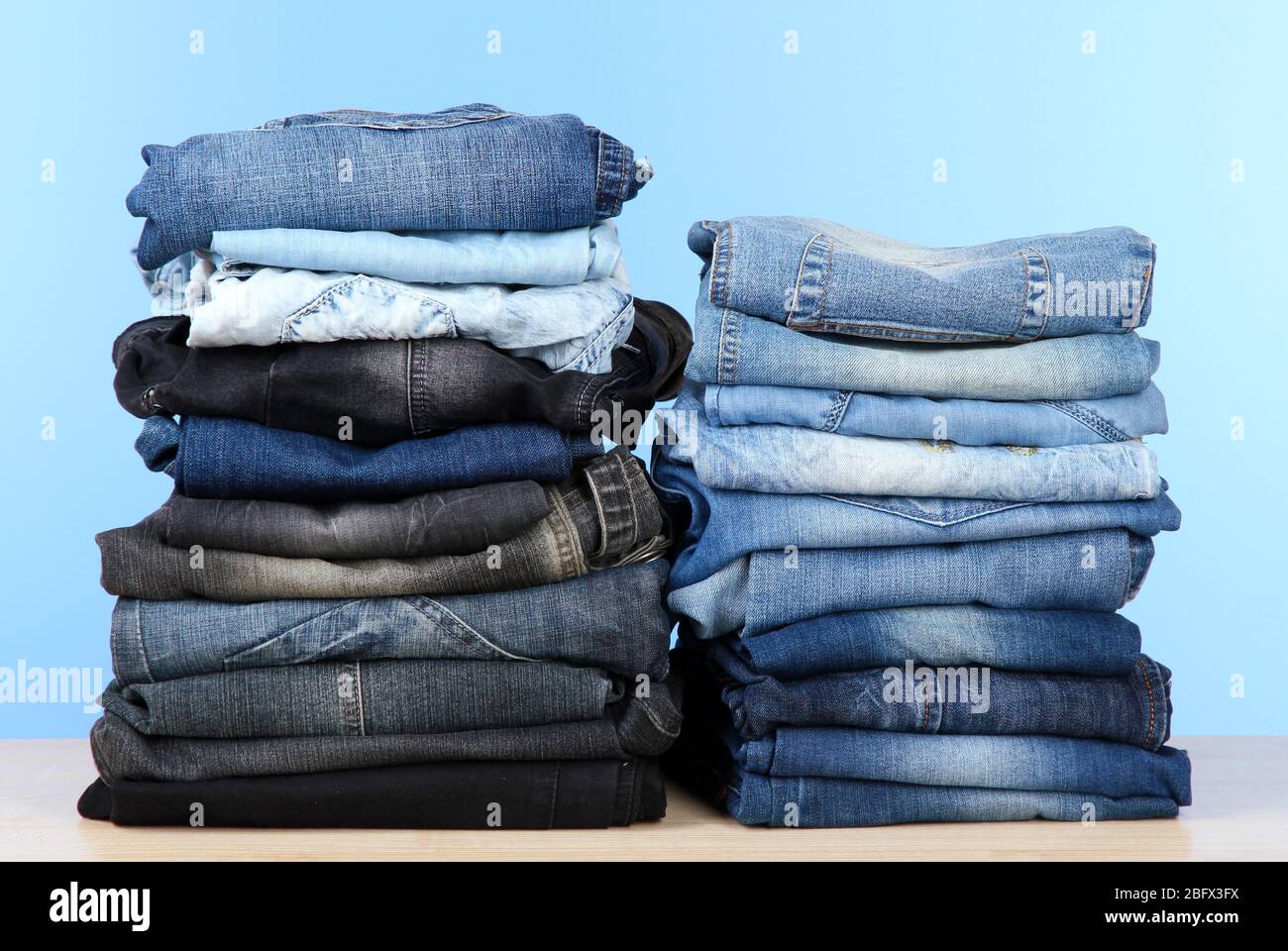 Many jeans stacked in a piles on blue background Stock Photo - Alamy