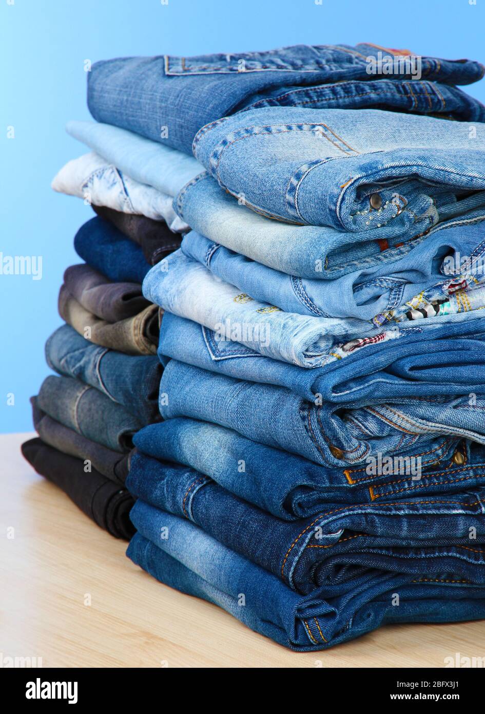 Many jeans stacked in a piles on blue background Stock Photo - Alamy