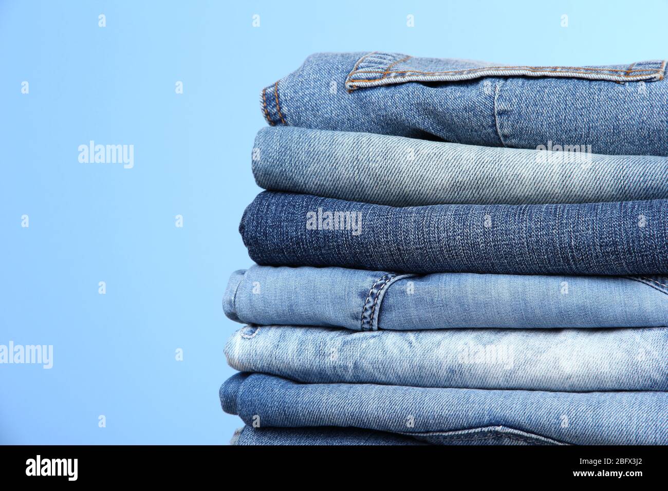 Many jeans stacked in a pile on blue background Stock Photo - Alamy