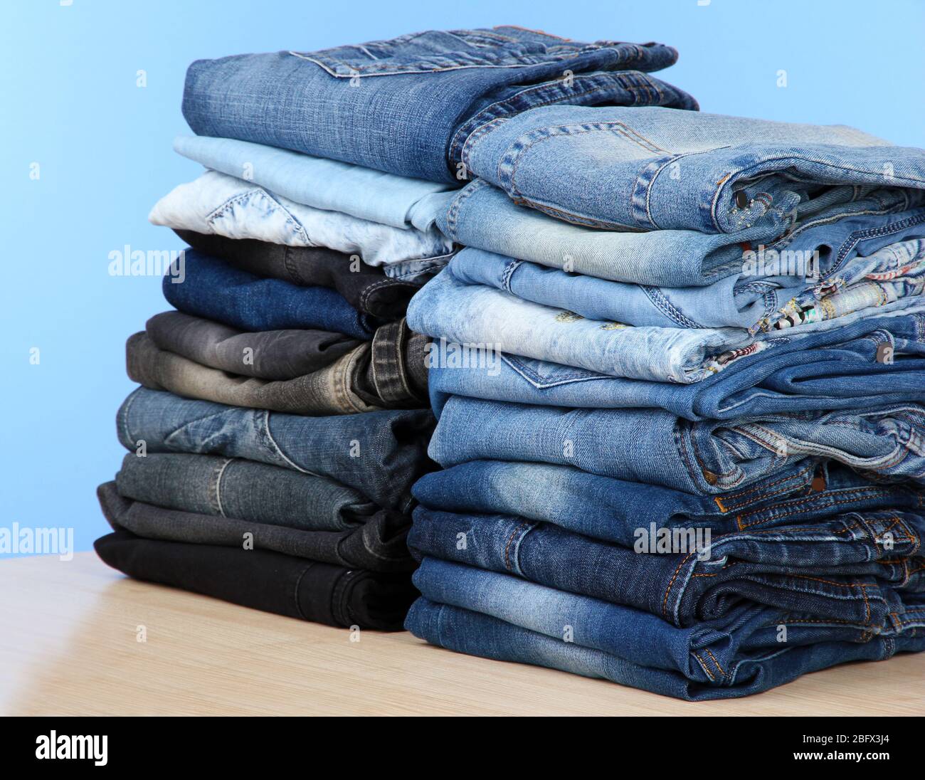 Many jeans stacked in a piles on blue background Stock Photo - Alamy