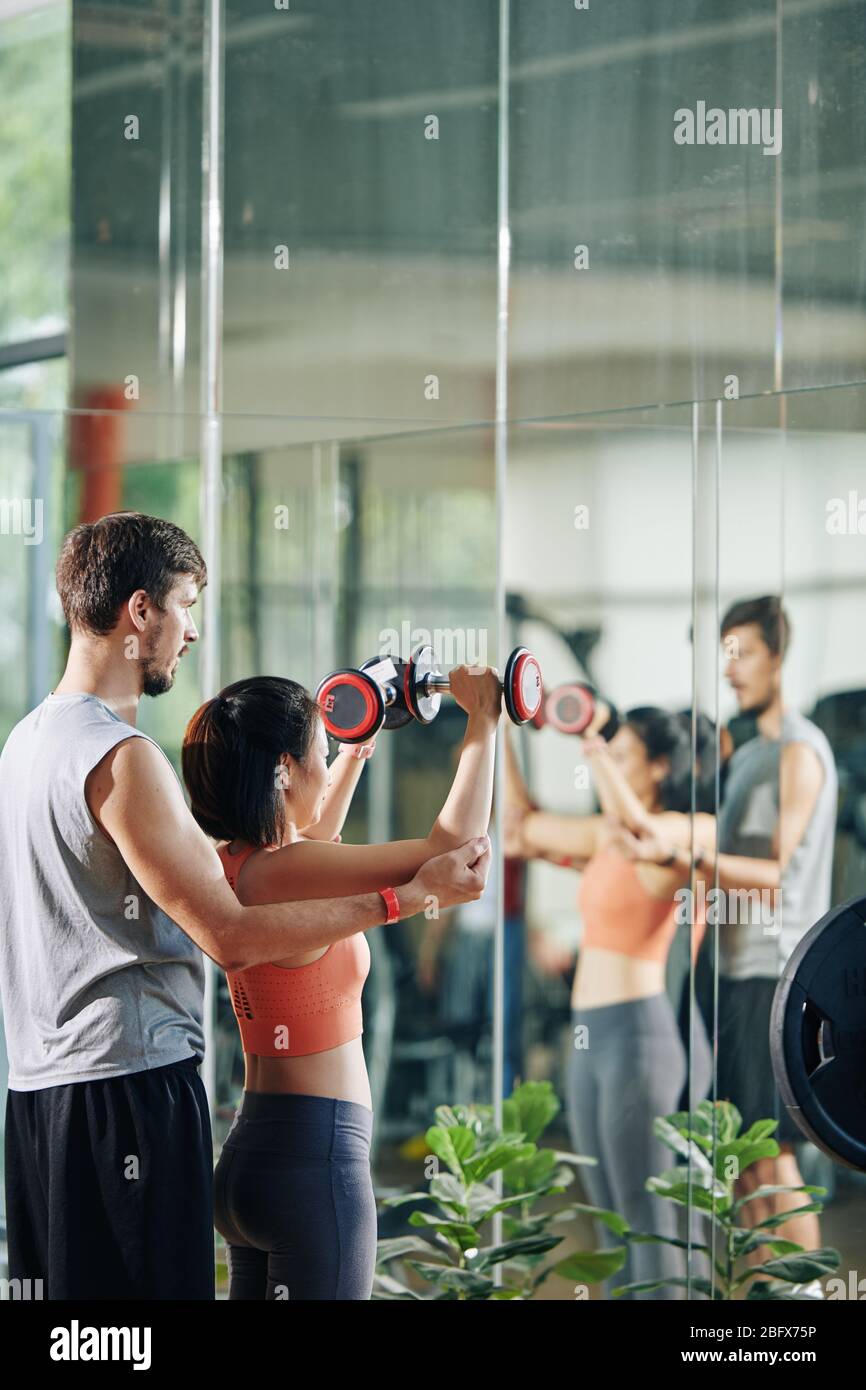 Fitness coach explaining young woman how to do lateral raise with ...