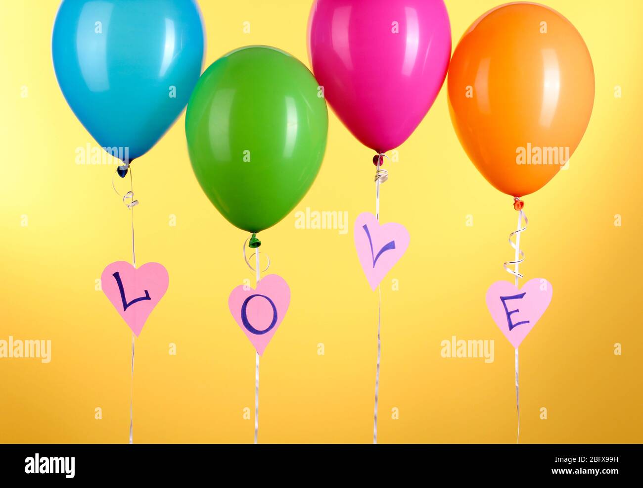 Colorful balloons keeps word love on yellow background Stock Photo - Alamy