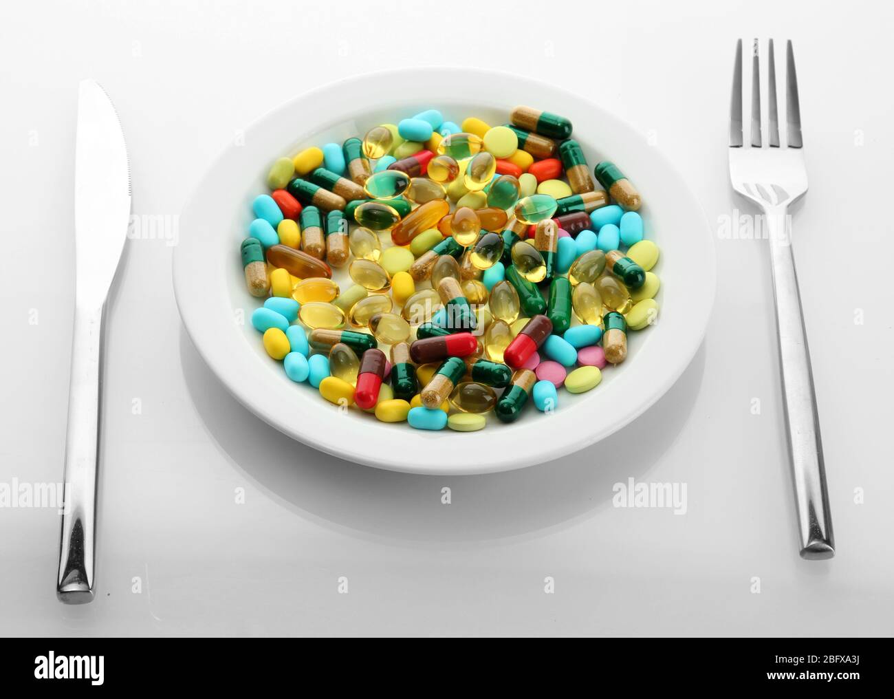 Colorful capsules and pills on plate with fork and knife, isolated on ...