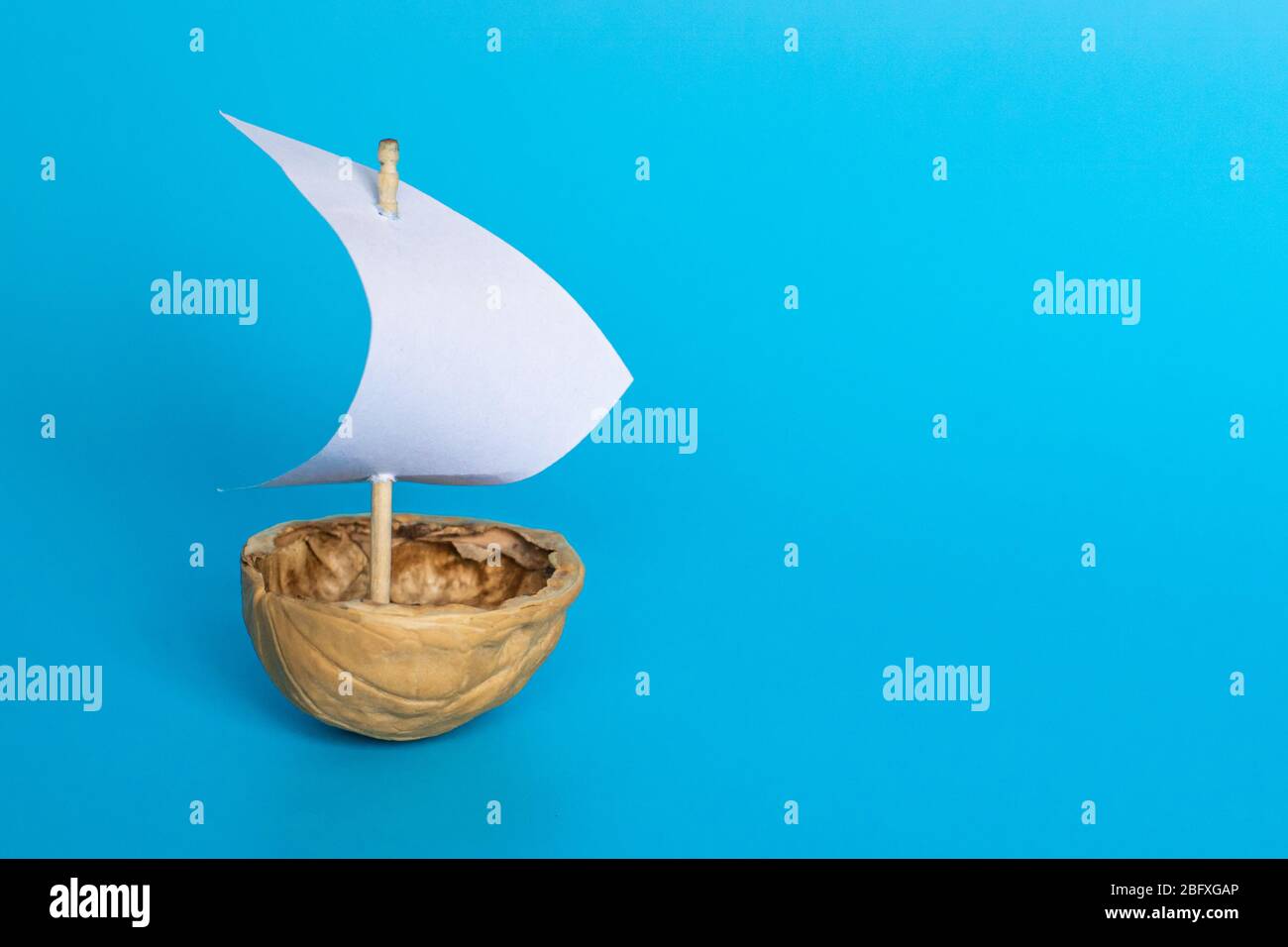 a boat made of nutshell with a white sail on the blue background ...