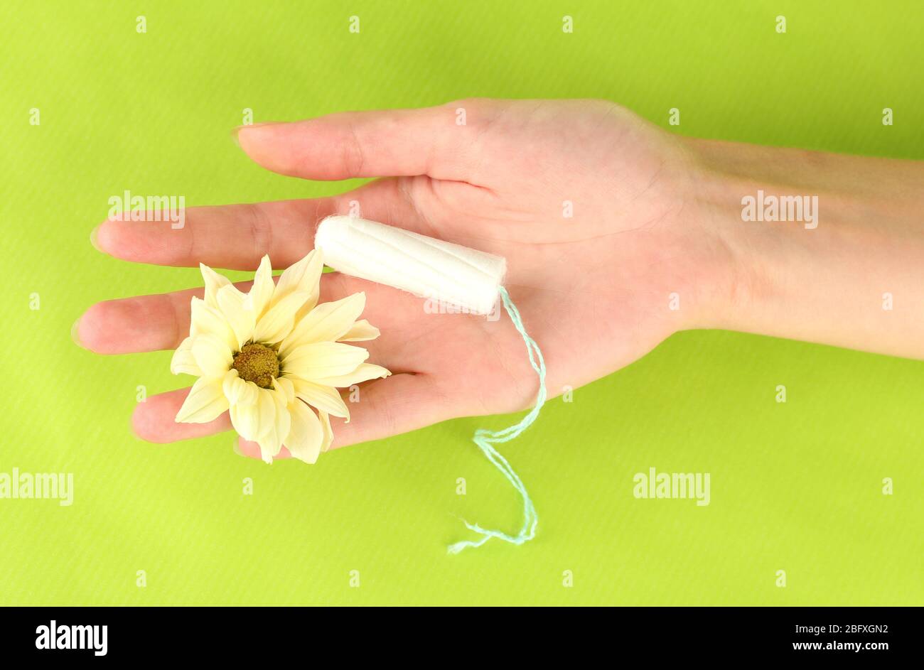 woman's hand holding a clean cotton tampon on green background close-up ...