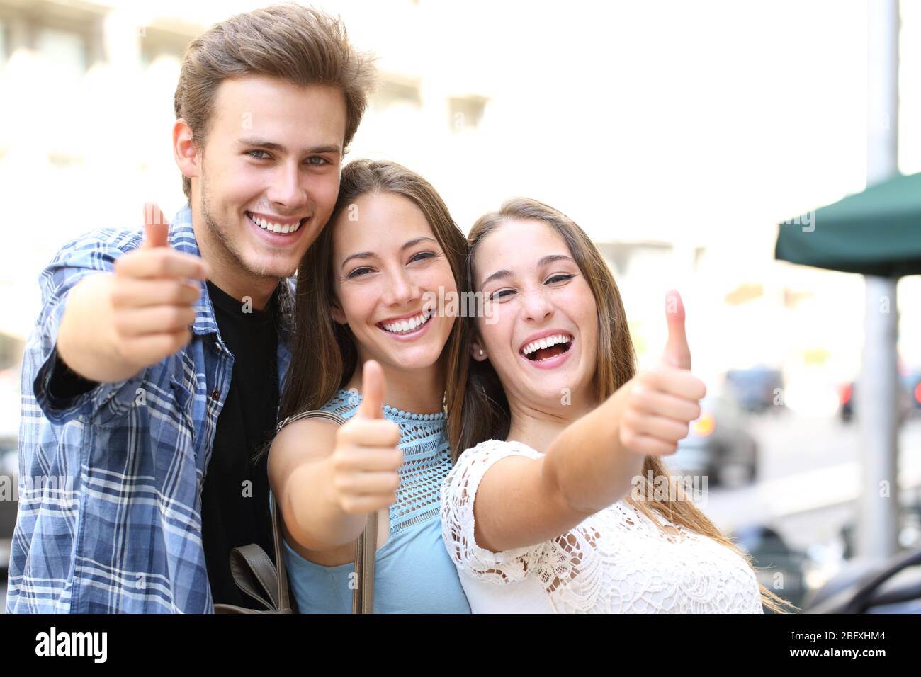 Happy group of three friends with thumbs up and perfect smiles looking ...