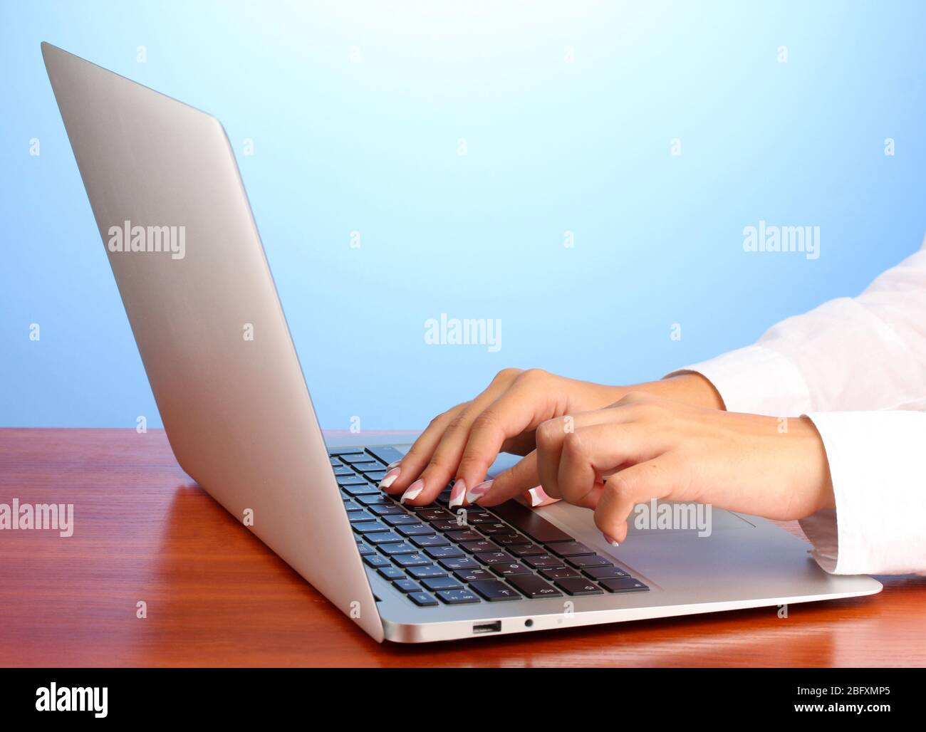 business woman's hands typing on laptop computer, on blue background ...